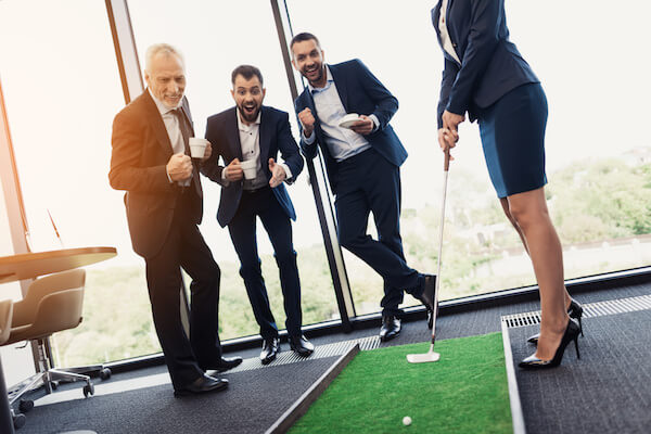 Three businessmen and business ladies play golf. A woman is holding a ...